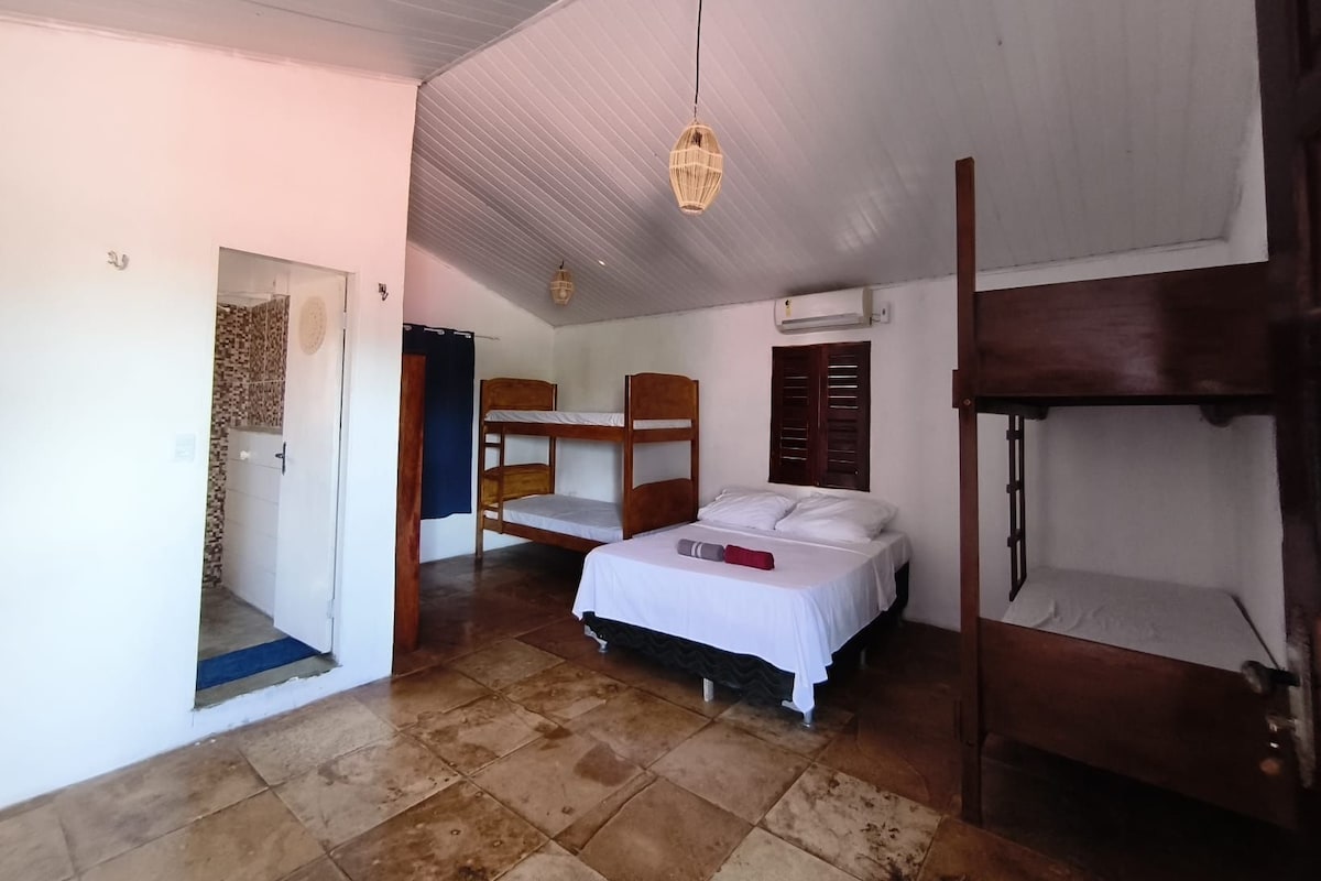 Quarto com beliches, porta de madeira, piso ladrilhado e luminária pendente.