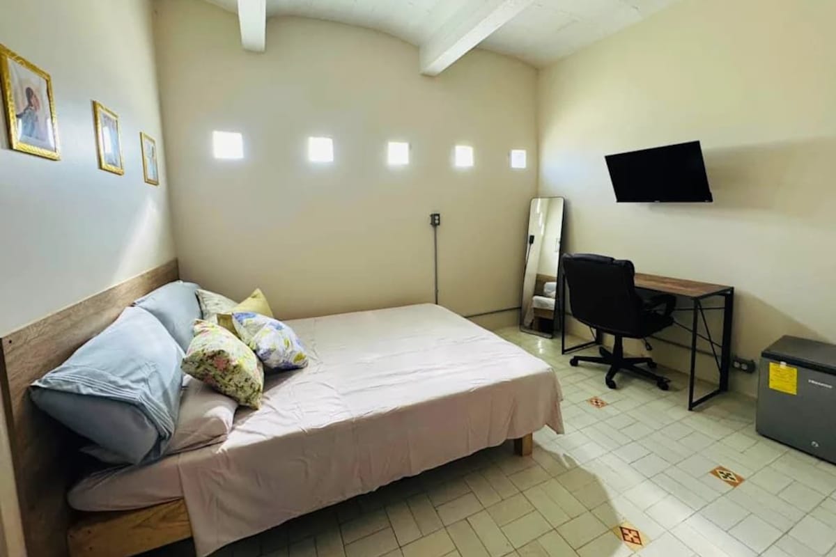 Quarto com cama, escrivaninha, cadeira, televisão e guarda-roupa.