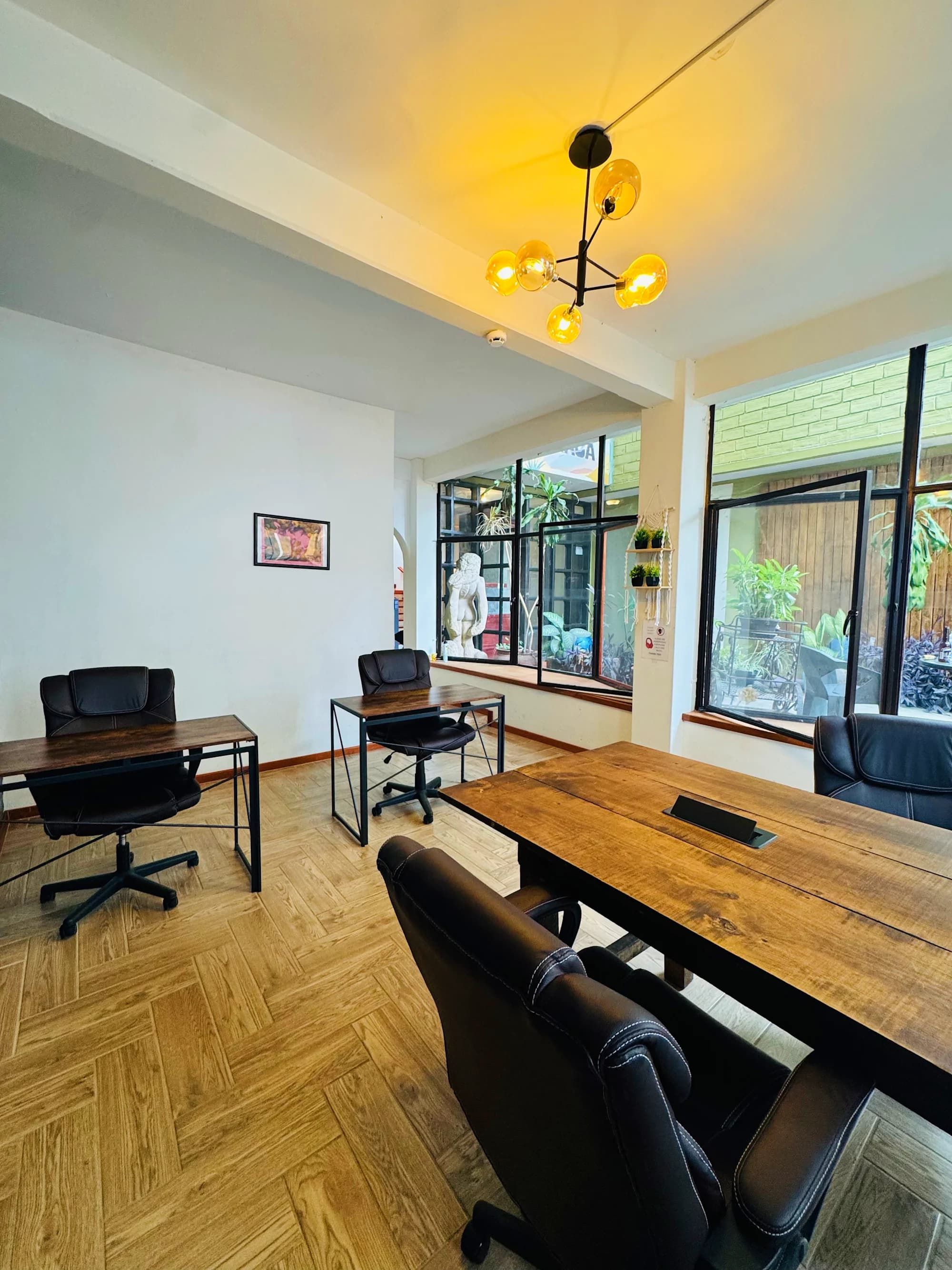 Uma sala de conferências com uma grande mesa de madeira, cadeiras de escritório pretas e um lustre no teto.