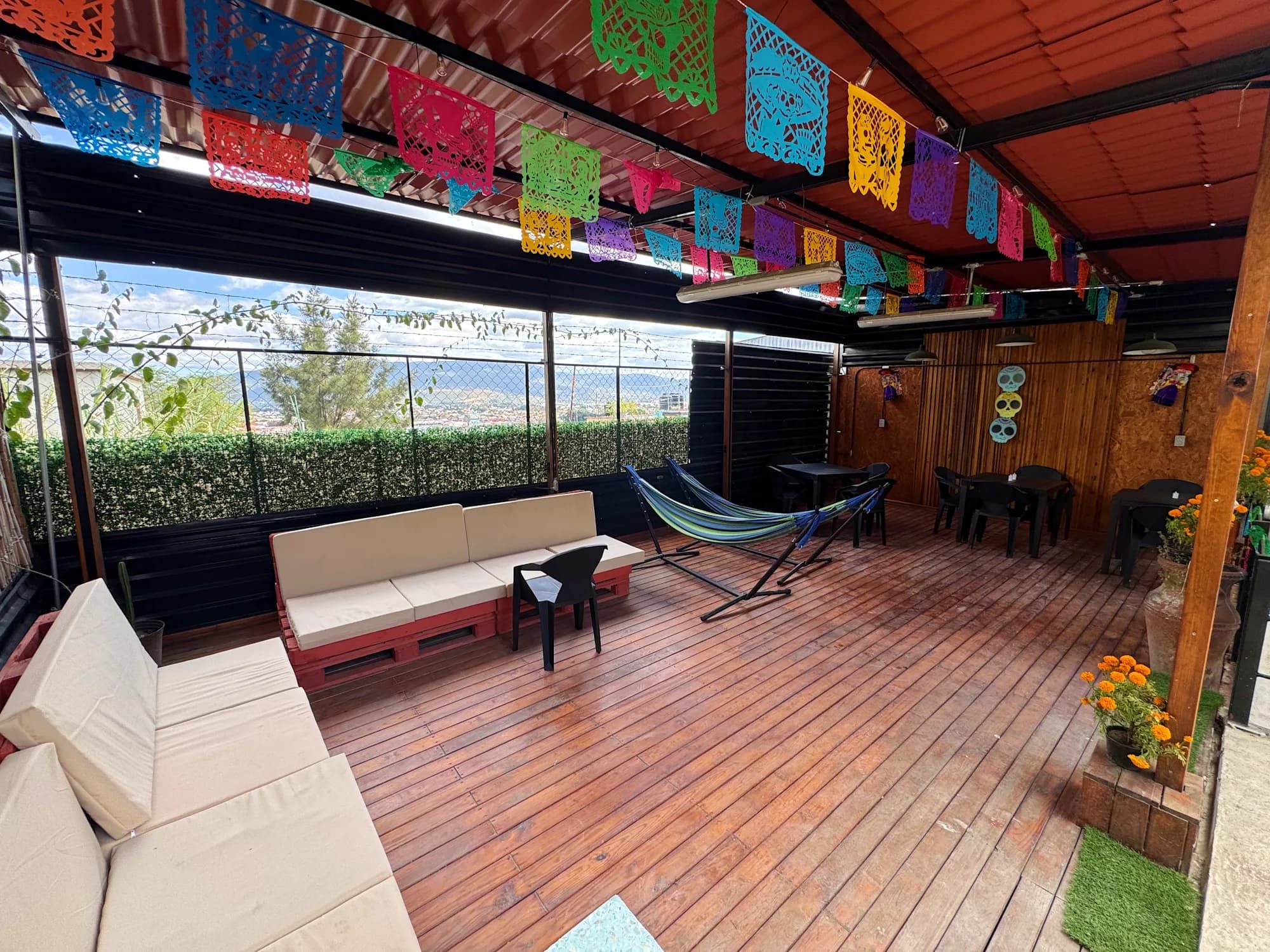 Um pátio externo com deck de madeira, um sofá branco, uma rede e vista para áreas verdes e edifícios.