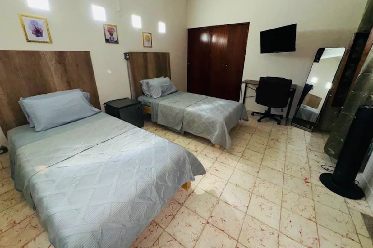 Quarto com duas camas, uma escrivaninha, uma cadeira, um guarda-roupa e uma TV de tela plana.