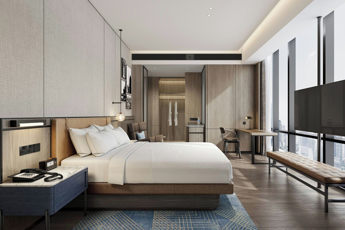Quarto de hotel moderno com uma cama grande, escrivaninha, televisão e vista para a cidade.