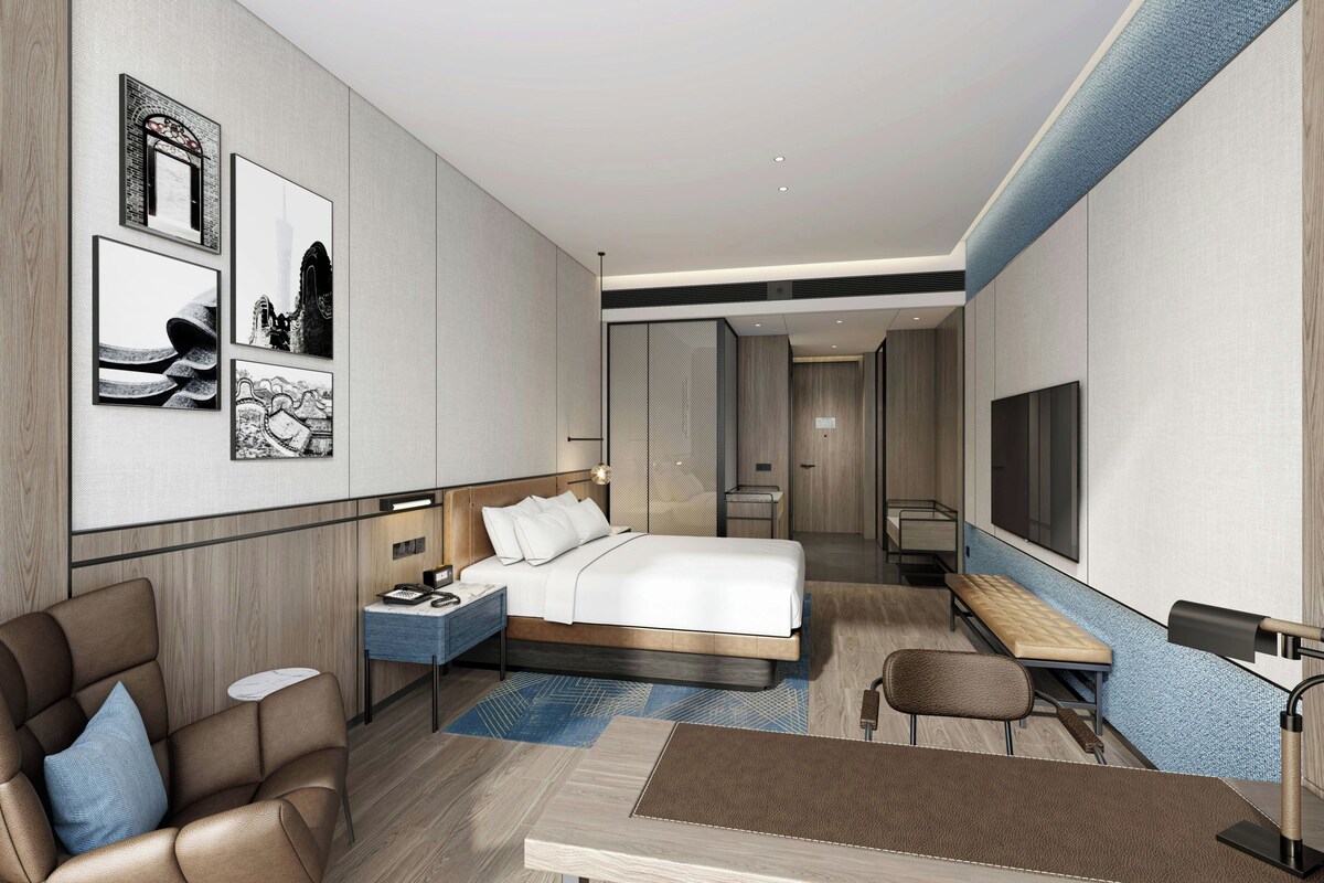 Quarto de hotel moderno com cama, área de estar e televisão.