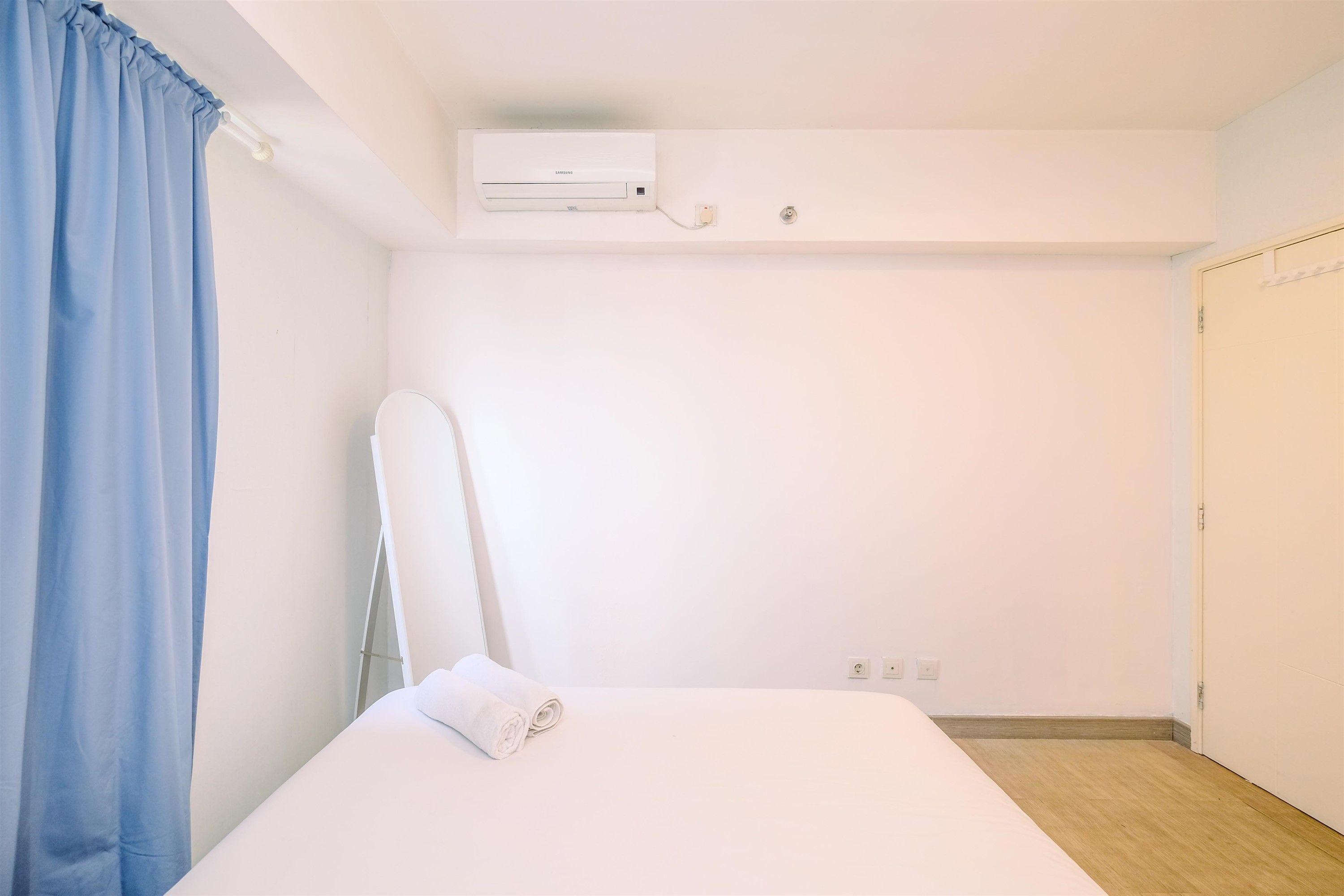 Quarto de hotel com cama, ar-condicionado na parede, porta e cortina.