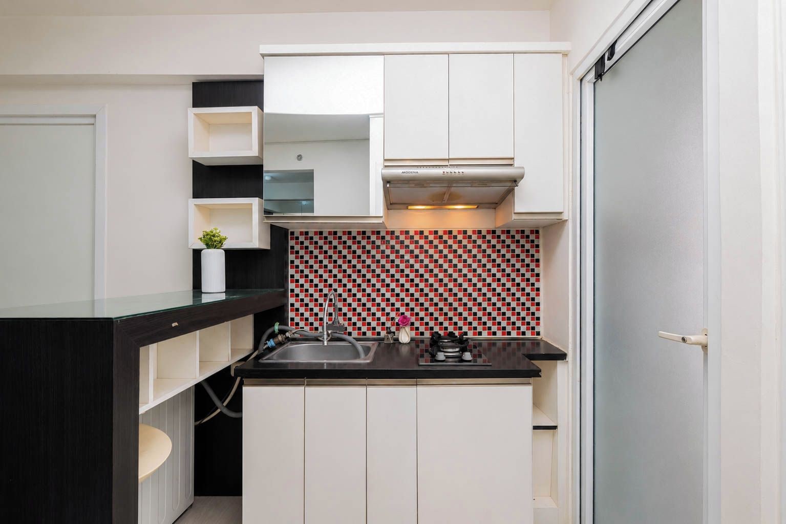 Cozinha compacta com armários brancos, bancada preta, painel de fundo estampado e fogão embutido.