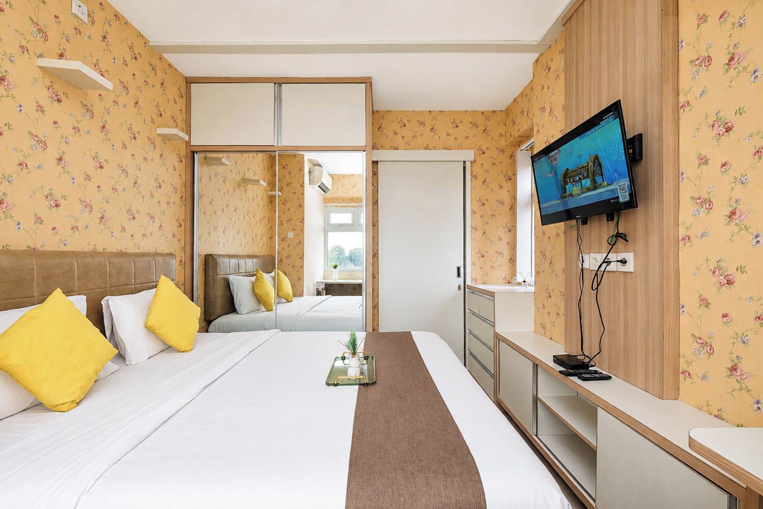 Quarto de hotel com cama, escrivaninha, televisão e guarda-roupa.