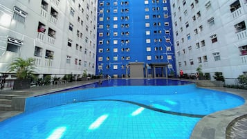 Piscina com pisos e paredes revestidas, rodeada por um edifício residencial com vários andares, varandas e janelas.