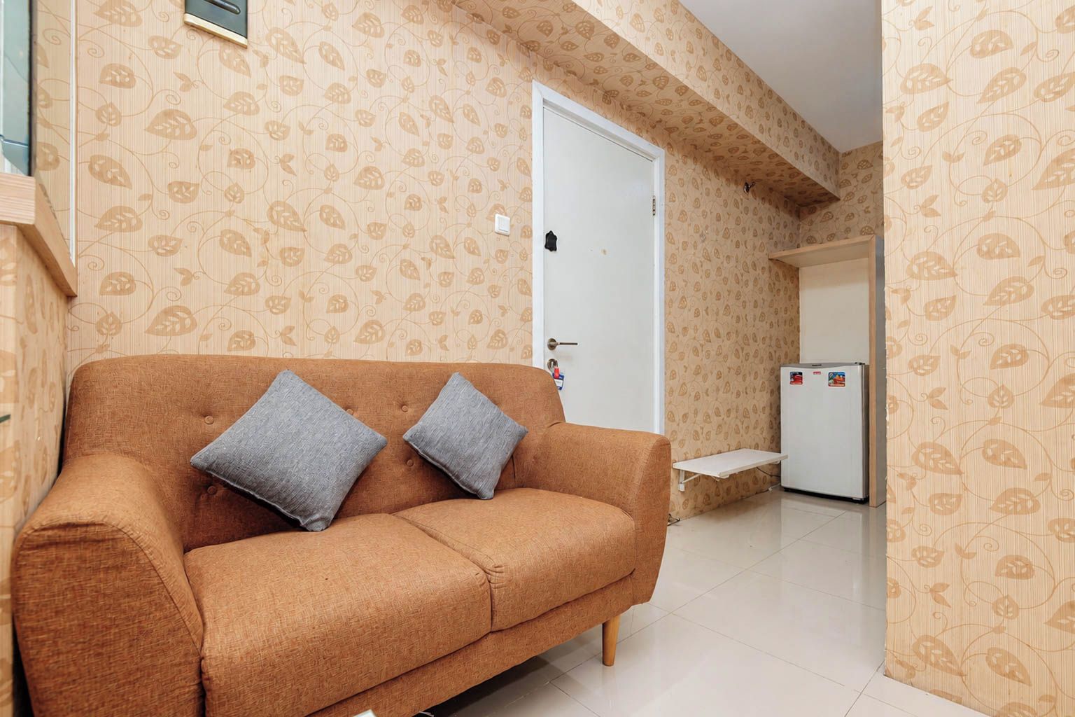 Quarto com sofá, porta e refrigerador.