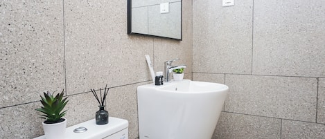 Um banheiro com pia branca, espelho, planta em vaso e vaso sanitário.