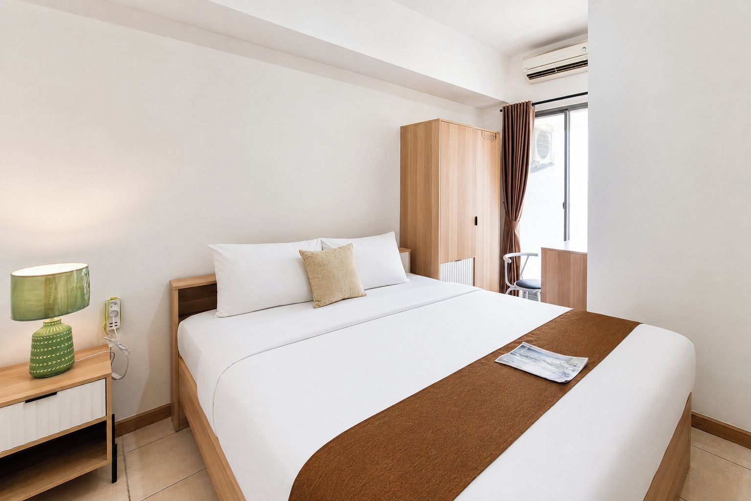 Quarto de hotel com cama, mesa de cabeceira, luminária, guarda-roupa e janela com cortinas.