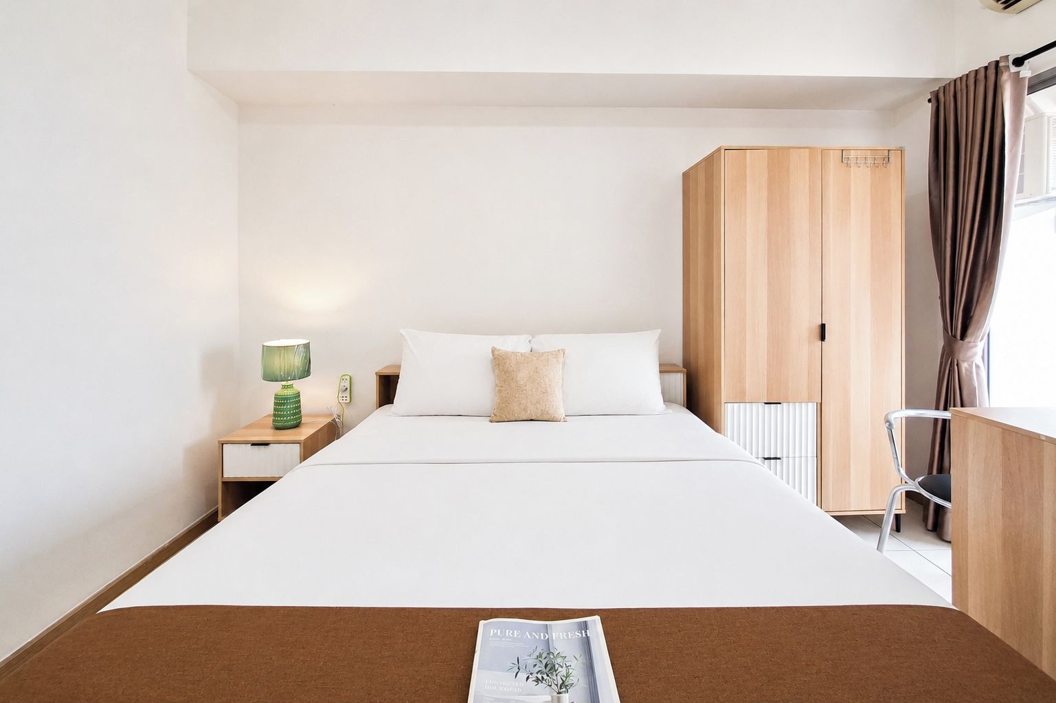 Quarto de hotel com cama, mesa de cabeceira, luminária, guarda-roupa e escrivaninha.