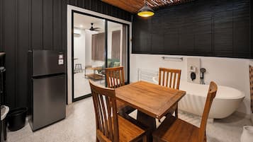 Cozinha compacta com geladeira, mesa de jantar de madeira, cadeiras e banheira com chuveiro.
