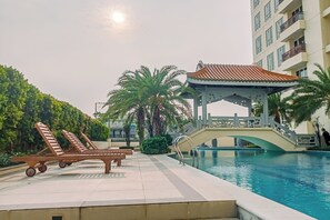 Uma área de piscina com espreguiçadeiras, um gazebo e uma ponte sobre a piscina.
