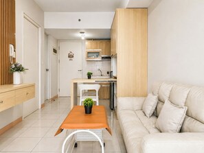 Sala de estar moderna com sofá e mesa de centro, cozinha com armários de madeira e micro-ondas, e corredor com porta.