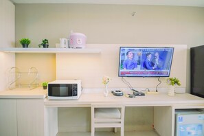 Uma cozinha compacta com micro-ondas, chaleira, uma pequena planta em vaso e uma televisão exibindo um noticiário.