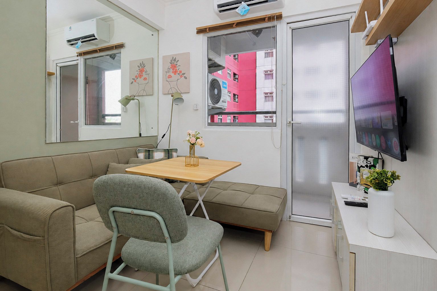 Uma sala de estar moderna com sofá, mesa pequena, cadeira, TV e janela com vista para um edifício.