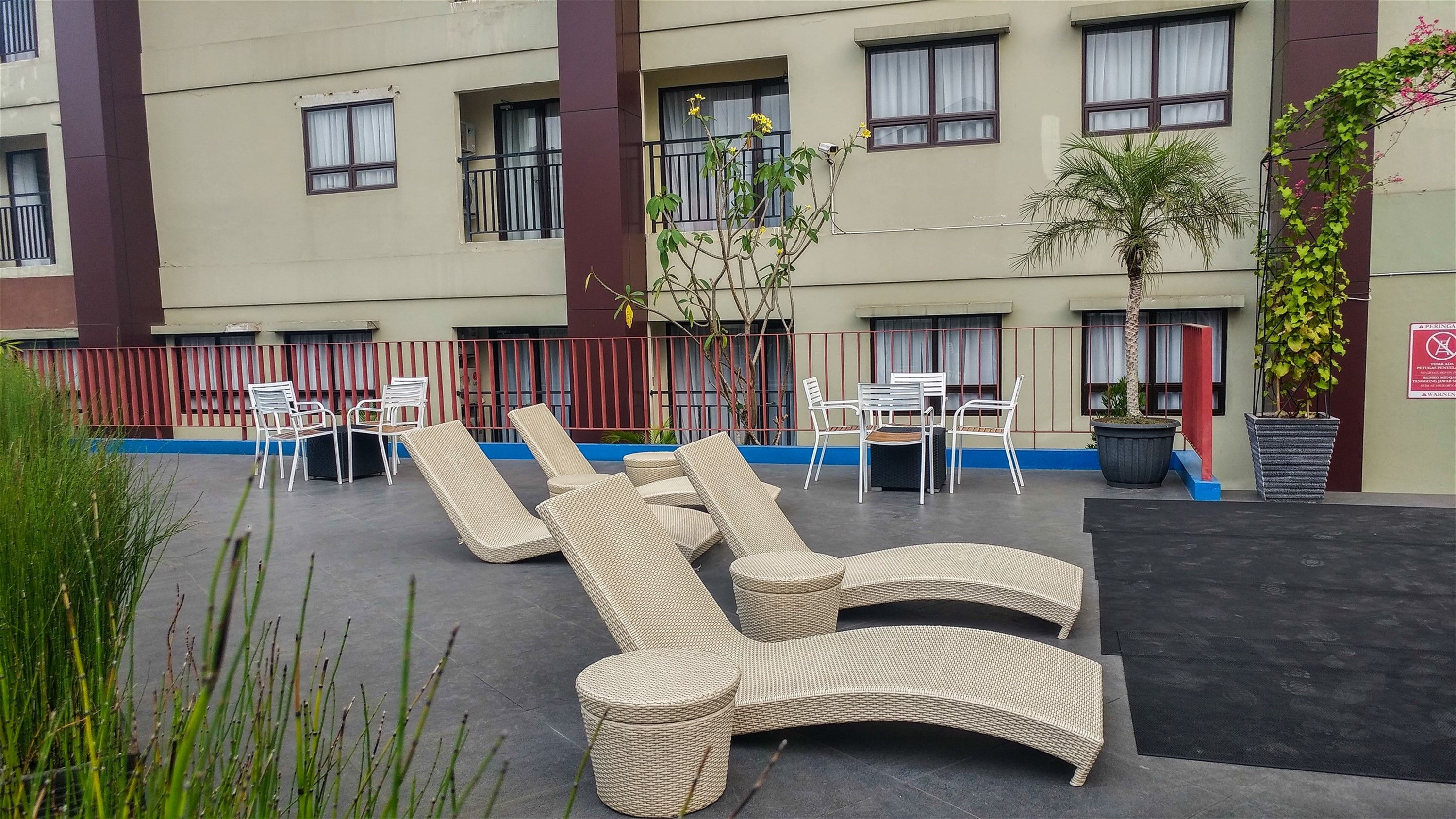 Terraço no telhado com espreguiçadeiras e mesas, cercado por um gradil baixo e plantas em vasos.