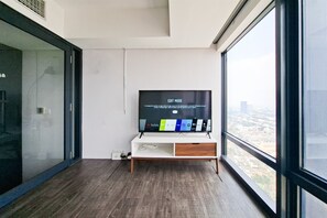 Quarto moderno com uma grande janela, TV de tela plana em um suporte branco e vista para a paisagem urbana.