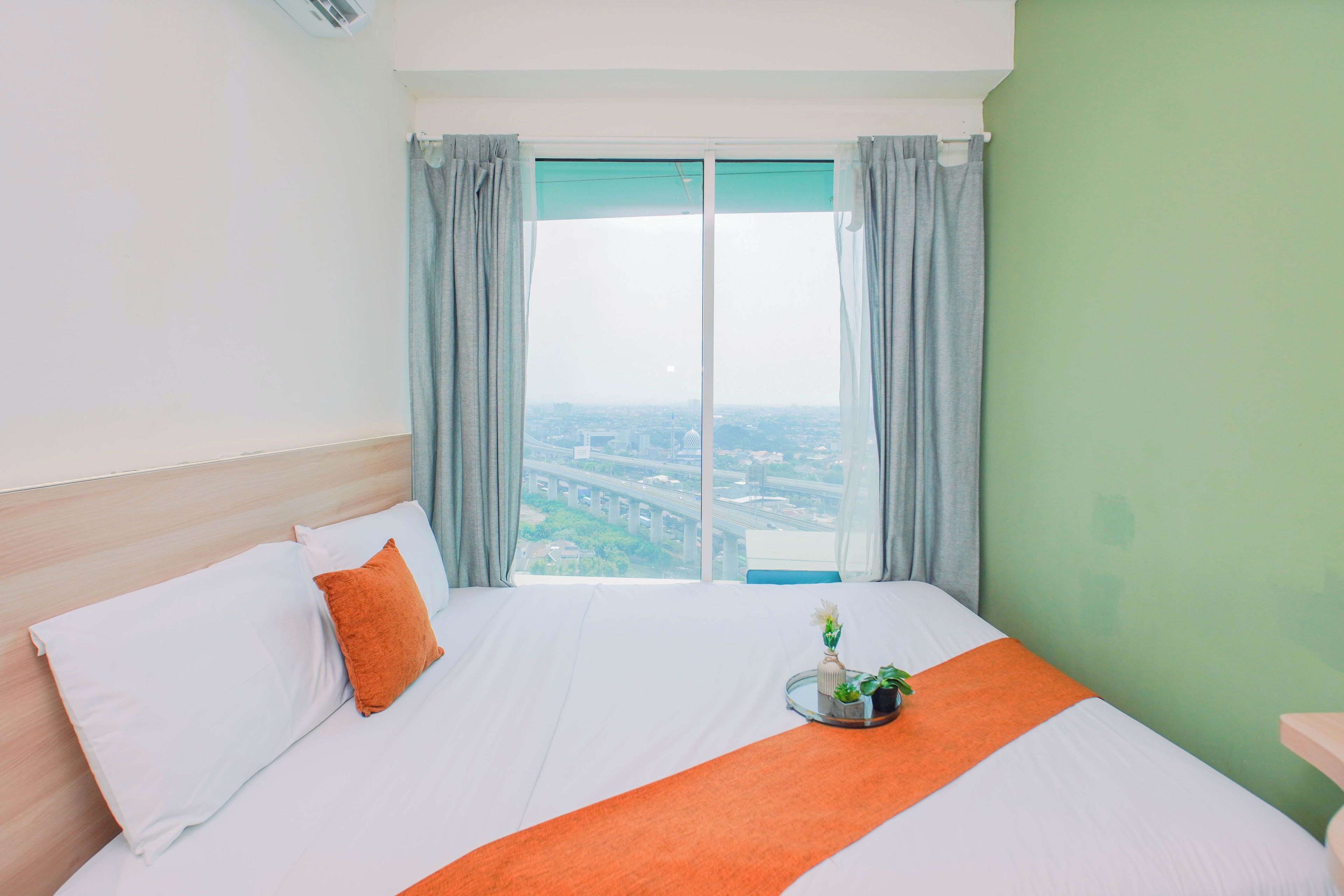Quarto de hotel com uma cama grande, vista para a cidade pela janela e uma mesinha com um vaso de flores.