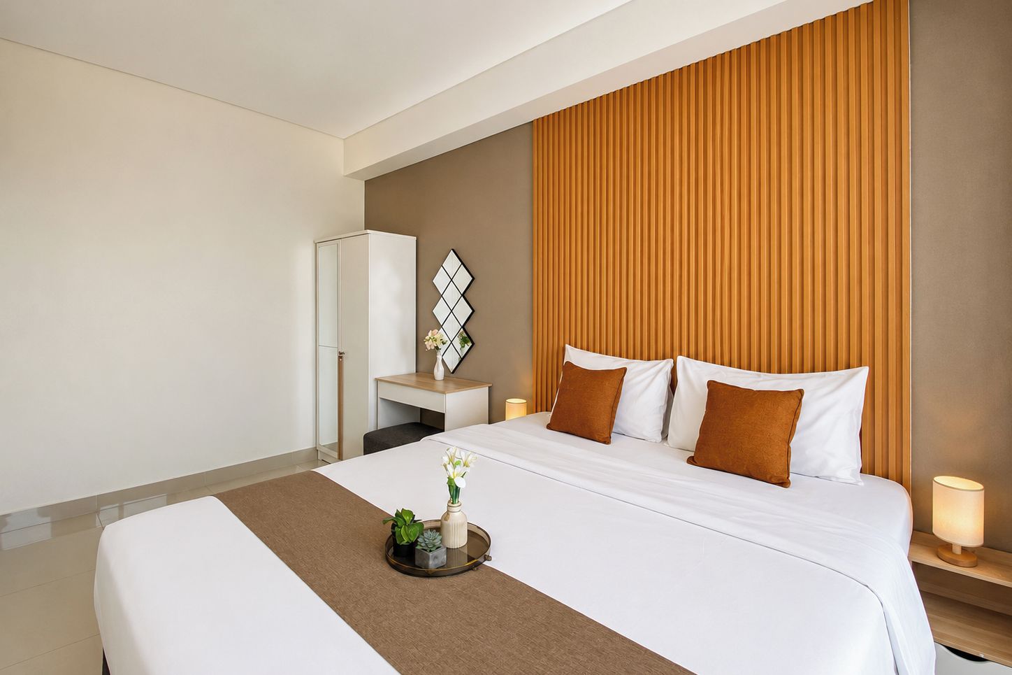 Quarto de hotel com uma cama grande, uma escrivaninha, um guarda-roupa e um painel decorativo na parede.