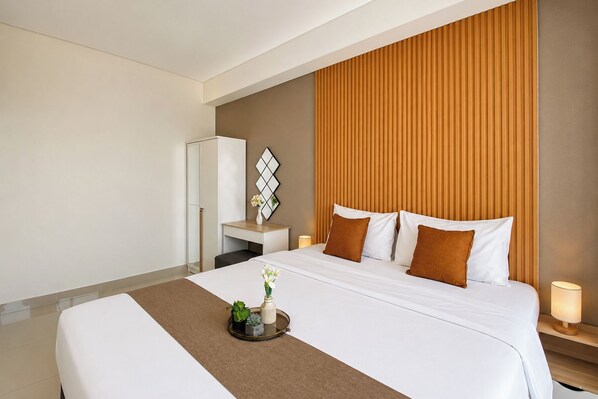 Quarto de hotel com uma cama grande, uma escrivaninha, um guarda-roupa e um painel decorativo na parede.