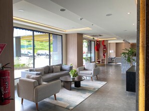 Um saguão de hotel moderno com um sofá, cadeiras, uma mesa de centro e um balcão de recepção.