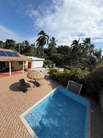 Piscina com espreguiçadeiras, área coberta com painéis solares e vegetação tropical exuberante.