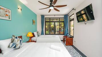 Quarto de hotel com duas camas, ventilador de teto, televisão fixada na parede e janela com cortinas.