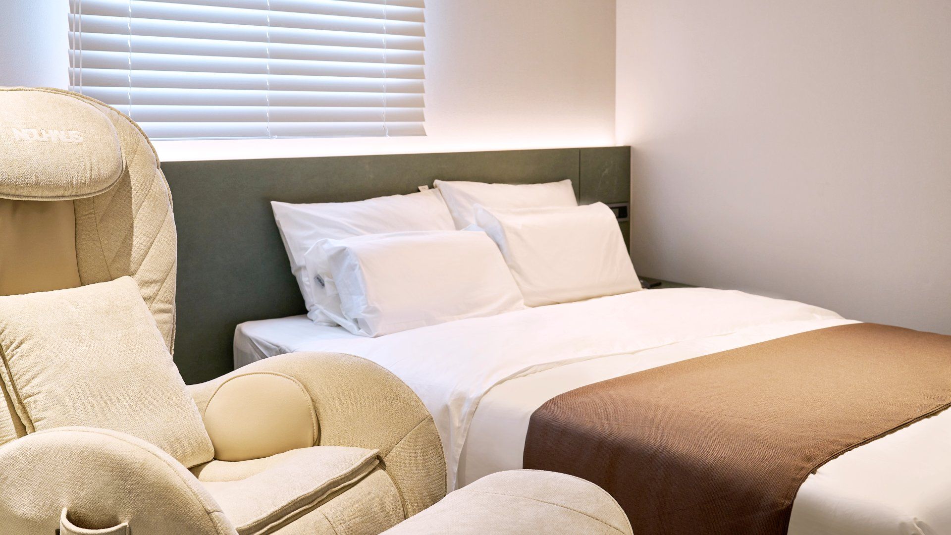 Quarto de hotel com uma cama, uma cadeira e uma janela com persianas.