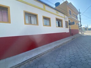 Um edifício com fachada vermelha e amarela, porta visível e rua pavimentada com azulejos hexagonais.