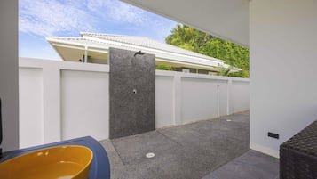 Área externa coberta com parede branca, coluna texturizada cinza e um objeto amarelo.