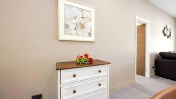 Quarto com penteadeira branca, uma pintura floral emoldurada na parede e uma porta que dá para outro cômodo.