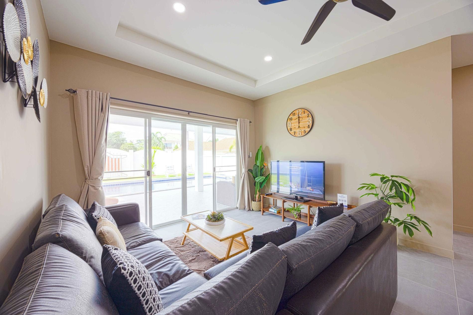 Uma sala de estar com sofá, mesa de centro, televisão e uma janela grande com cortinas.