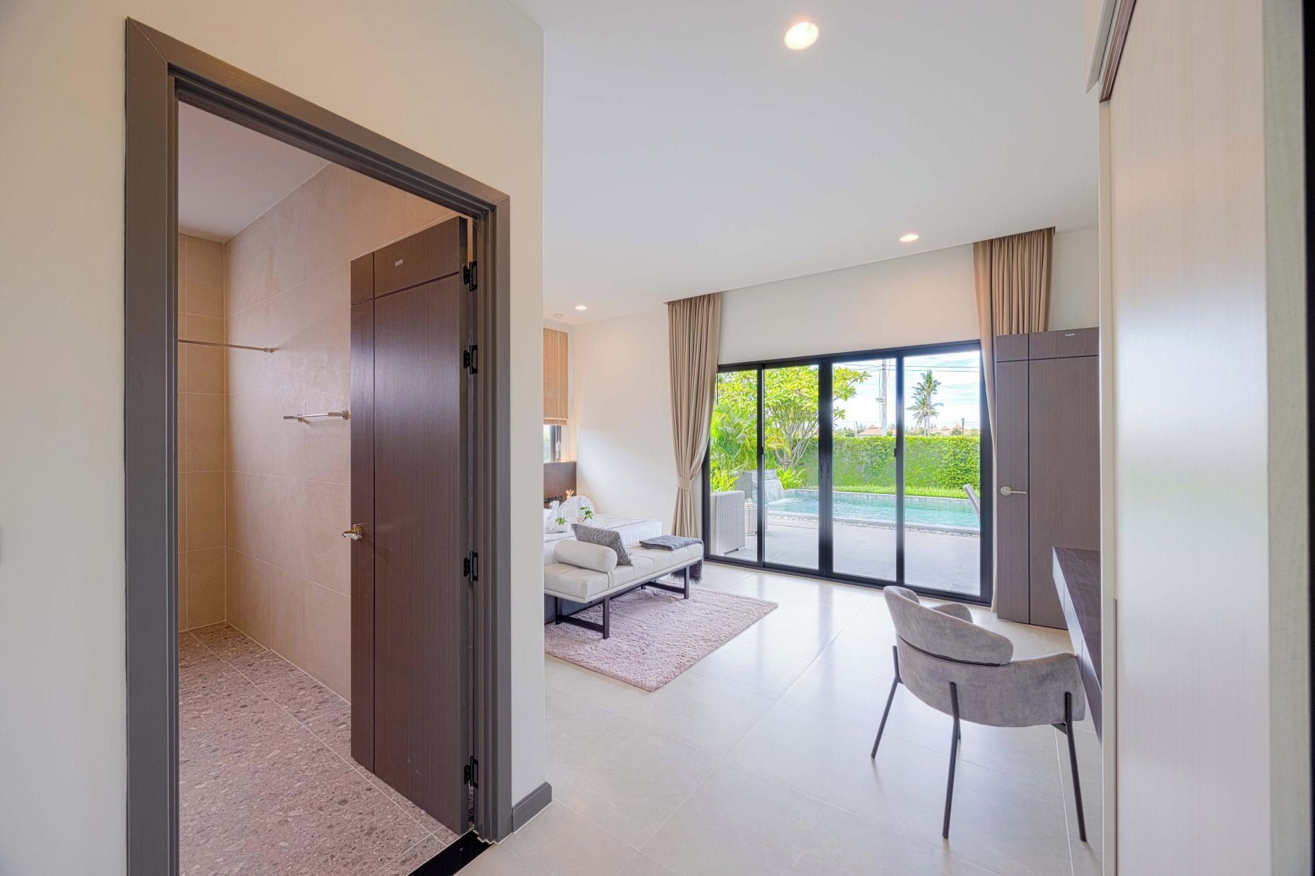 Quarto de hotel moderno com uma grande porta de vidro deslizante que dá para uma varanda, um sofá, uma cadeira e uma pequena mesa.