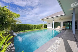 Uma casa moderna com piscina, varanda coberta e vista para o céu.
