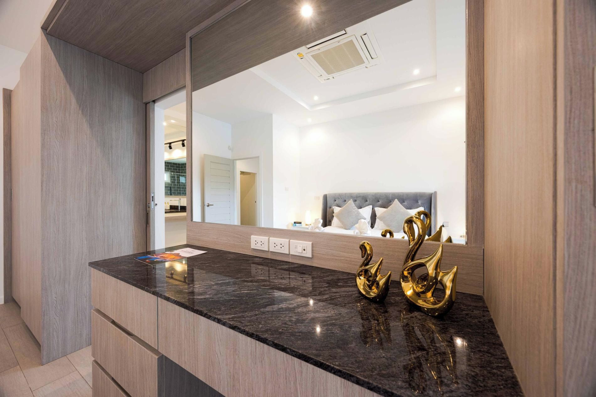 Casa de banho moderna com um espelho grande, bancada de mármore e um objeto decorativo dourado.