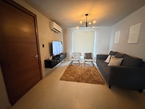 Uma sala de estar com sofá, televisão, lareira e janela.