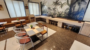 Uma sala de jantar moderna com uma mesa central, cadeiras e um banco. Há uma pintura grande na parede retratando paisagens tropicais.
