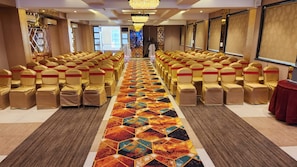 Uma sala de conferências com fileiras de cadeiras, um corredor com carpete e um palco na frente.
