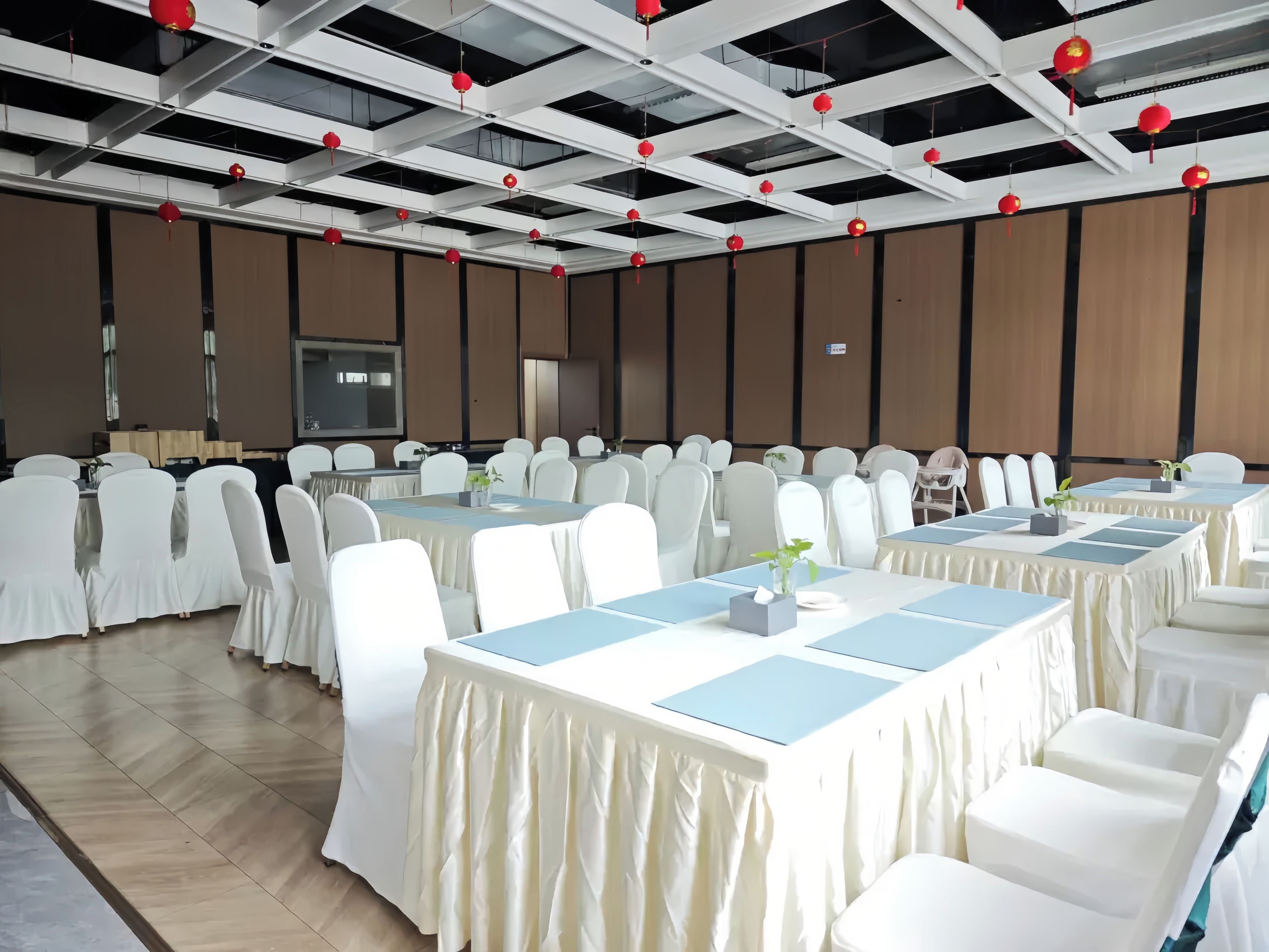 Sala de conferências com cadeiras brancas, mesas e decorações pendentes vermelhas.