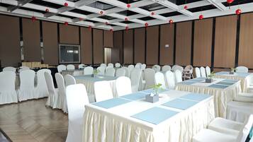 Sala de conferências com cadeiras brancas, mesas e decorações pendentes vermelhas.