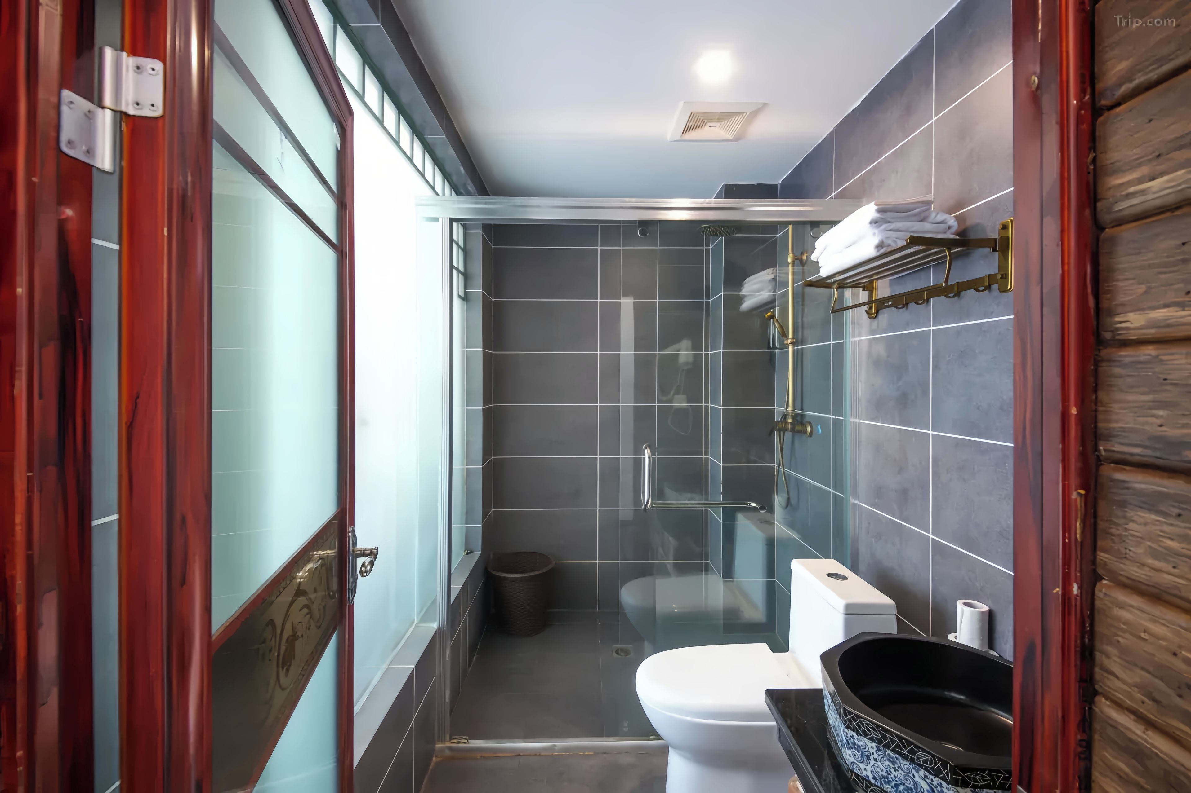 Casa de banho compacta com cabine de duche em vidro, sanita branca e lavatório preto com cuba decorativa.