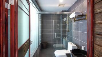 Casa de banho compacta com cabine de duche em vidro, sanita branca e lavatório preto com cuba decorativa.