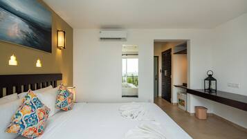 Quarto de hotel com cama, travesseiros, um quadro, mesa de cabeceira, espelho e vista para o mar.