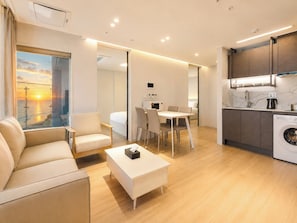 Uma sala de estar moderna com sofá, mesa de centro e área de jantar com cadeiras. Há vista para o oceano por uma grande janela.