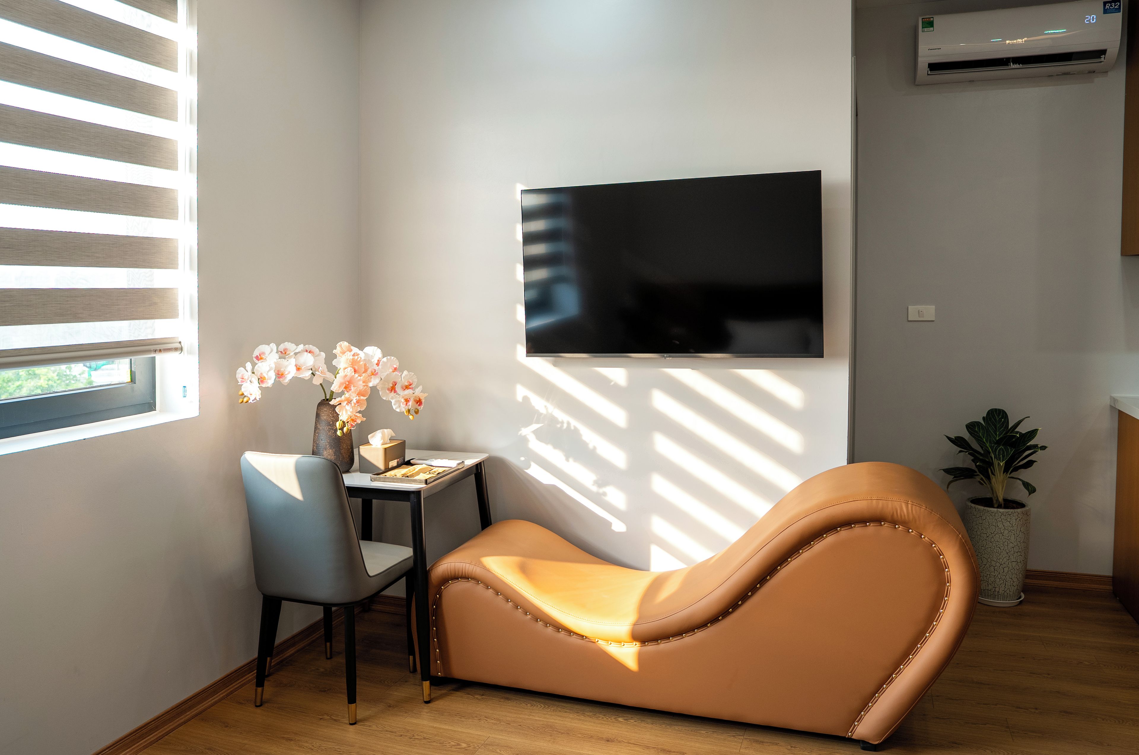 Uma sala de estar moderna com um sofá, uma mesa pequena com um vaso de flores, uma televisão na parede e um aparelho de ar condicionado.