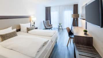 Quarto de hotel com duas camas, uma escrivaninha, uma cadeira, televisão e janela com cortinas.