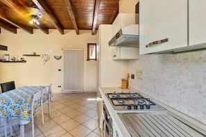 Cozinha com fogão a gás, armários brancos, painel de azulejos e teto de madeira.