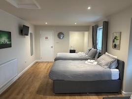 Quarto de hotel com duas camas, um radiador, um relógio, uma televisão e uma janela com cortinas.