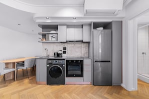 Uma cozinha compacta com máquina de lavar embutida, geladeira e área de refeições com mesa e cadeiras.